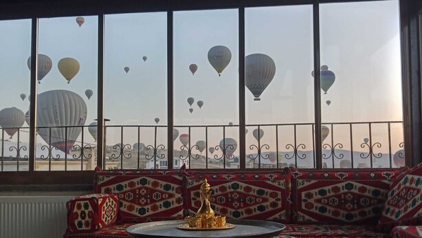 Quarto com uma grande janela com vista para um festival de balões.