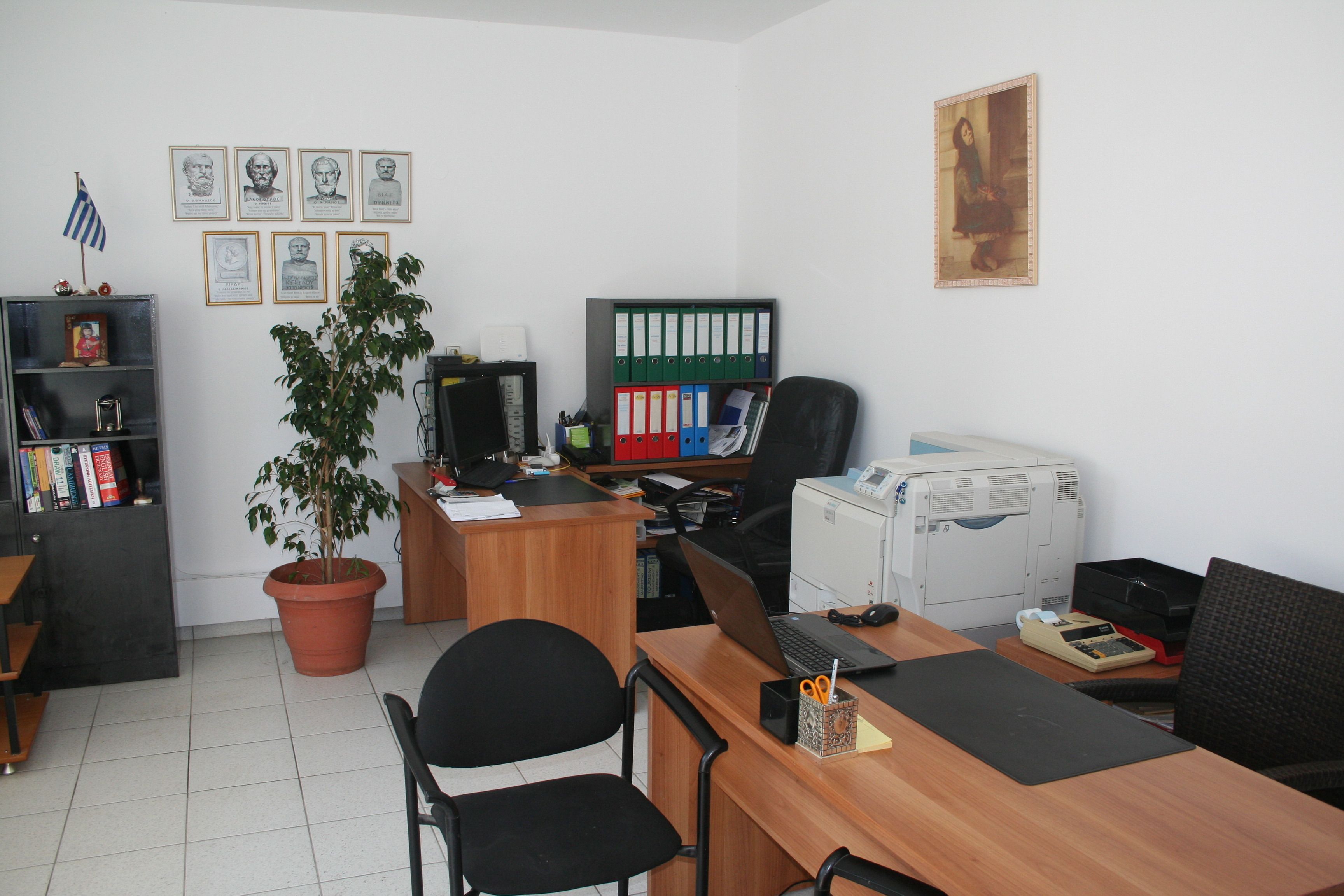 Escritório em casa com escrivaninha, computador, impressora, estante de livros e uma planta em vaso.