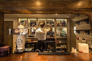 Um bar com um bartender preparando bebidas, prateleiras cheias de garrafas de licor e uma torneira de cerveja.
