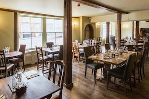 Um restaurante com mesas e cadeiras de madeira, janelas amplas e uma parede de tijolos.
