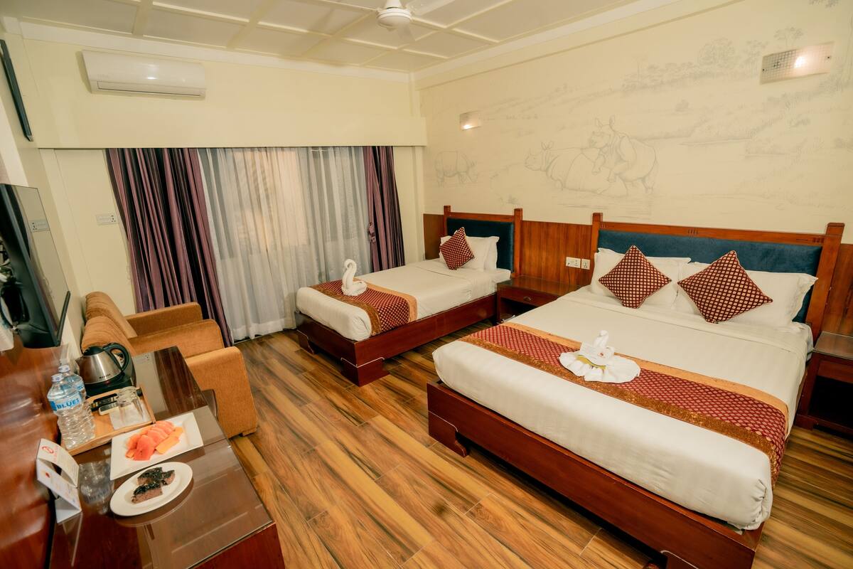 Quarto de hotel com duas camas, uma mesa de escritório com um laptop, uma cafeteira e um prato de comida.