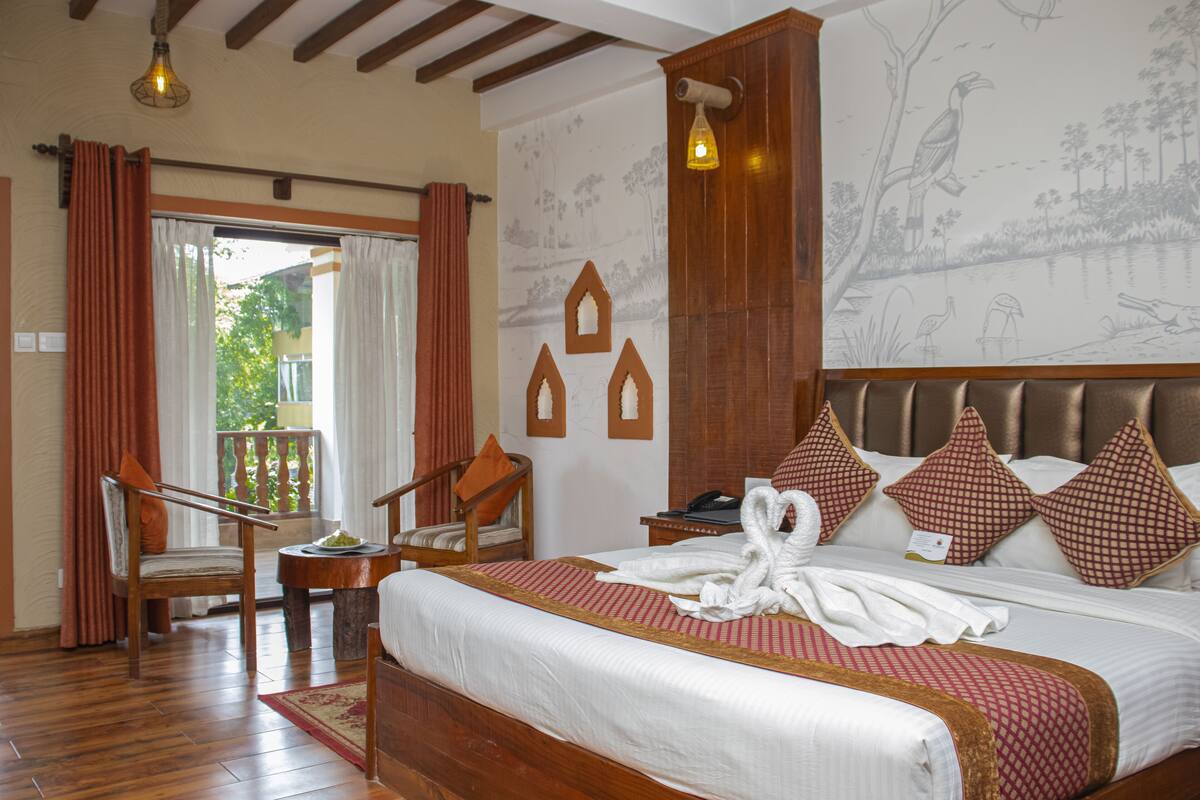Quarto de hotel com cama de madeira, varanda com cortinas, cadeira de madeira e painel na parede com tema de natureza.