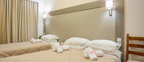 Quarto de hotel com duas camas, roupa de cama bege, almofadas brancas e uma cadeira de madeira.