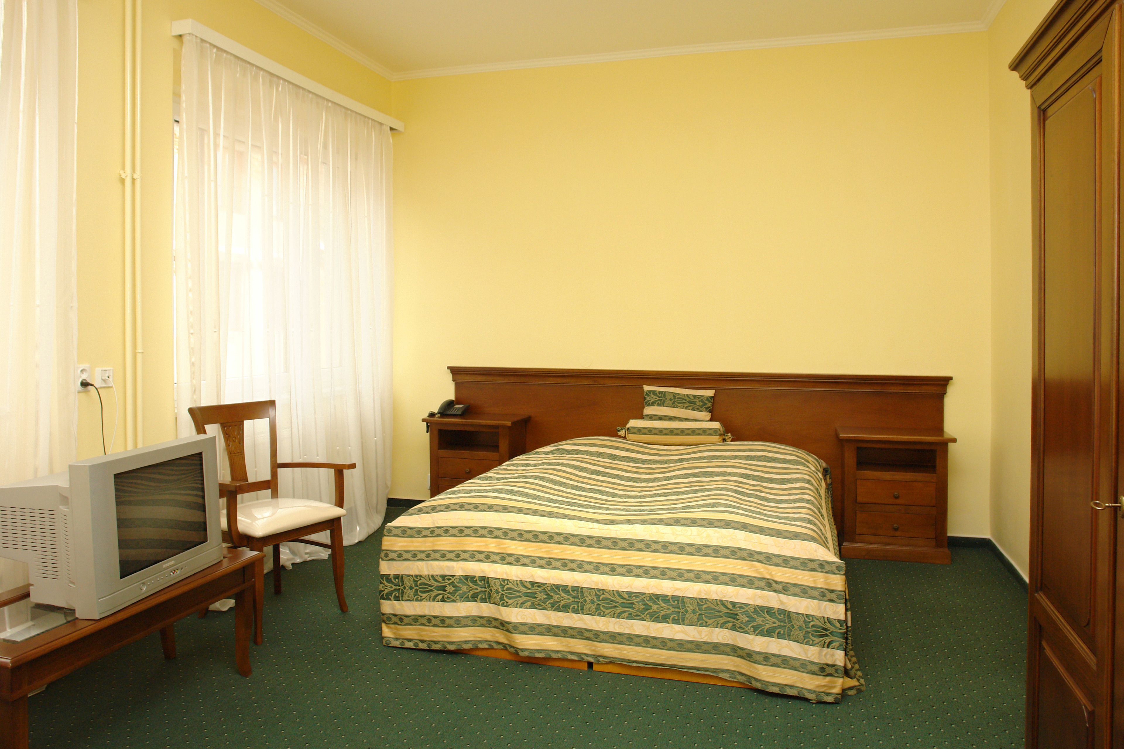 Quarto de hotel com uma cama, televisão, cadeira e guarda-roupa.