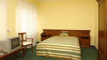Quarto de hotel com uma cama, televisão, cadeira e guarda-roupa.