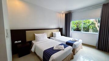 Quarto de hotel com duas camas, uma mesa de cabeceira, janela com cortinas e vista para o verde lá fora.