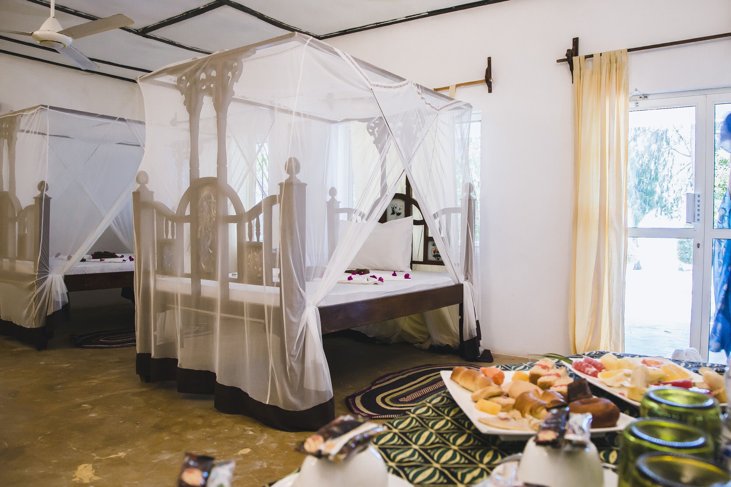 Quarto com duas camas, cada uma com dossel, e uma mesa de jantar com comida e bebidas.