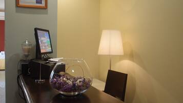 Um quarto com uma mesa de madeira, uma tigela de vidro com flores, uma luminária e um certificado emoldurado na parede.