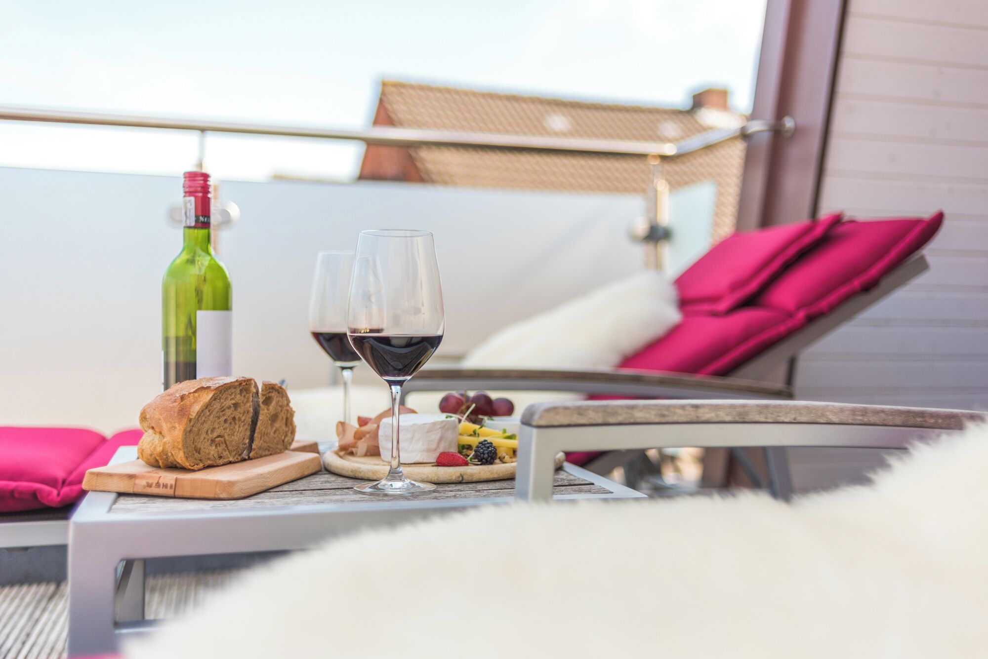 Uma mesa posta com uma garrafa de vinho, dois copos, um pão e uma tábua de queijos.