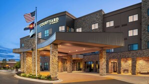 Hotel Courtyard by Marriott com fachada de pedra, entrada ampla e bandeira americana.