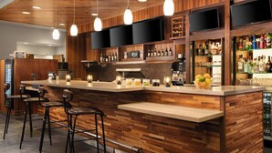 Uma área de bar com detalhes em madeira, banquetas e uma variedade de garrafas.