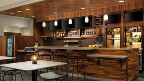 Uma área de bar moderna com painéis de madeira, banquetas e uma variedade de garrafas de bebidas.