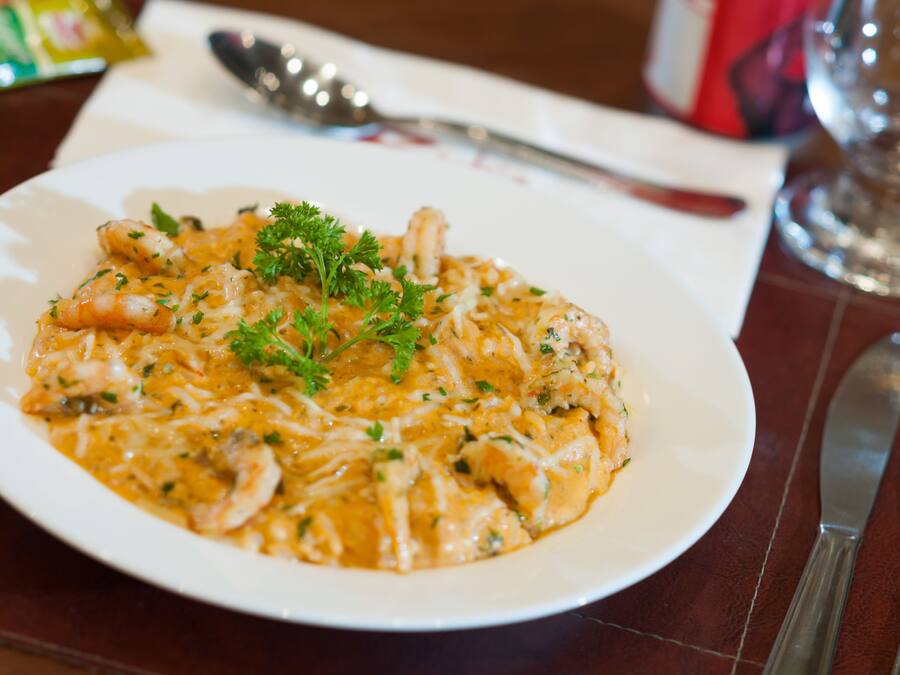 Um prato de massa com molho cremoso, decorado com salsa, sobre um prato branco.