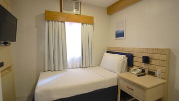 Quarto de hotel com cama, mesa de cabeceira com telefone, garrafa de água e televisão montada na parede.