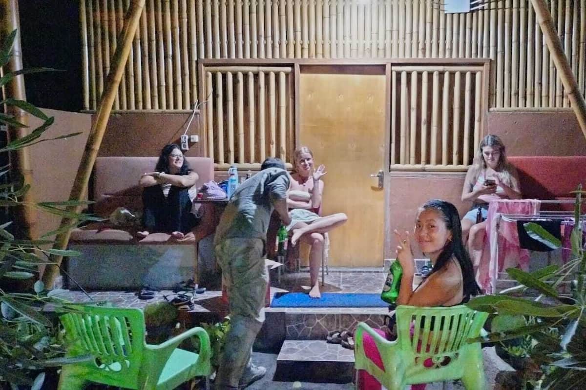 Um grupo de pessoas sentadas numa varanda com guarda-corrimão de bambu, rodeadas por vegetação.