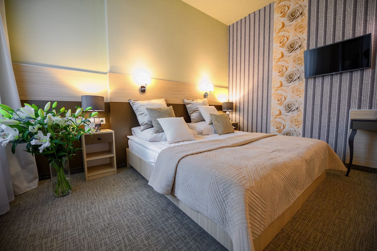 Quarto de hotel com uma cama grande, mesas de cabeceira, uma televisão e um vaso de flores.