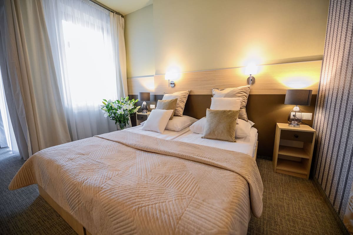 Quarto de hotel com uma cama grande, duas mesas de cabeceira e uma janela com cortinas.