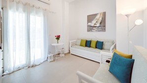 Um quarto claro e arejado com um sofá, uma mesinha com um vaso e um quadro de um veleiro na parede.