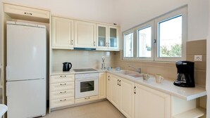 Uma cozinha com armários brancos, geladeira, forno, pia e janela com vista.