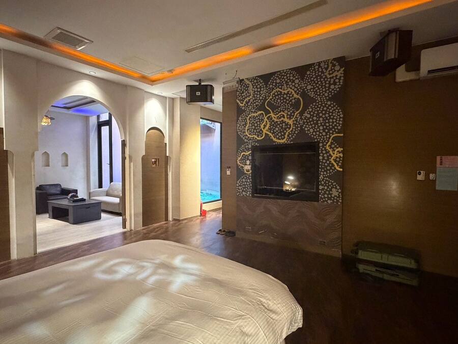 Quarto de hotel com uma cama grande, televisão fixada na parede e um espaço de estar com sofá e mesa de centro.