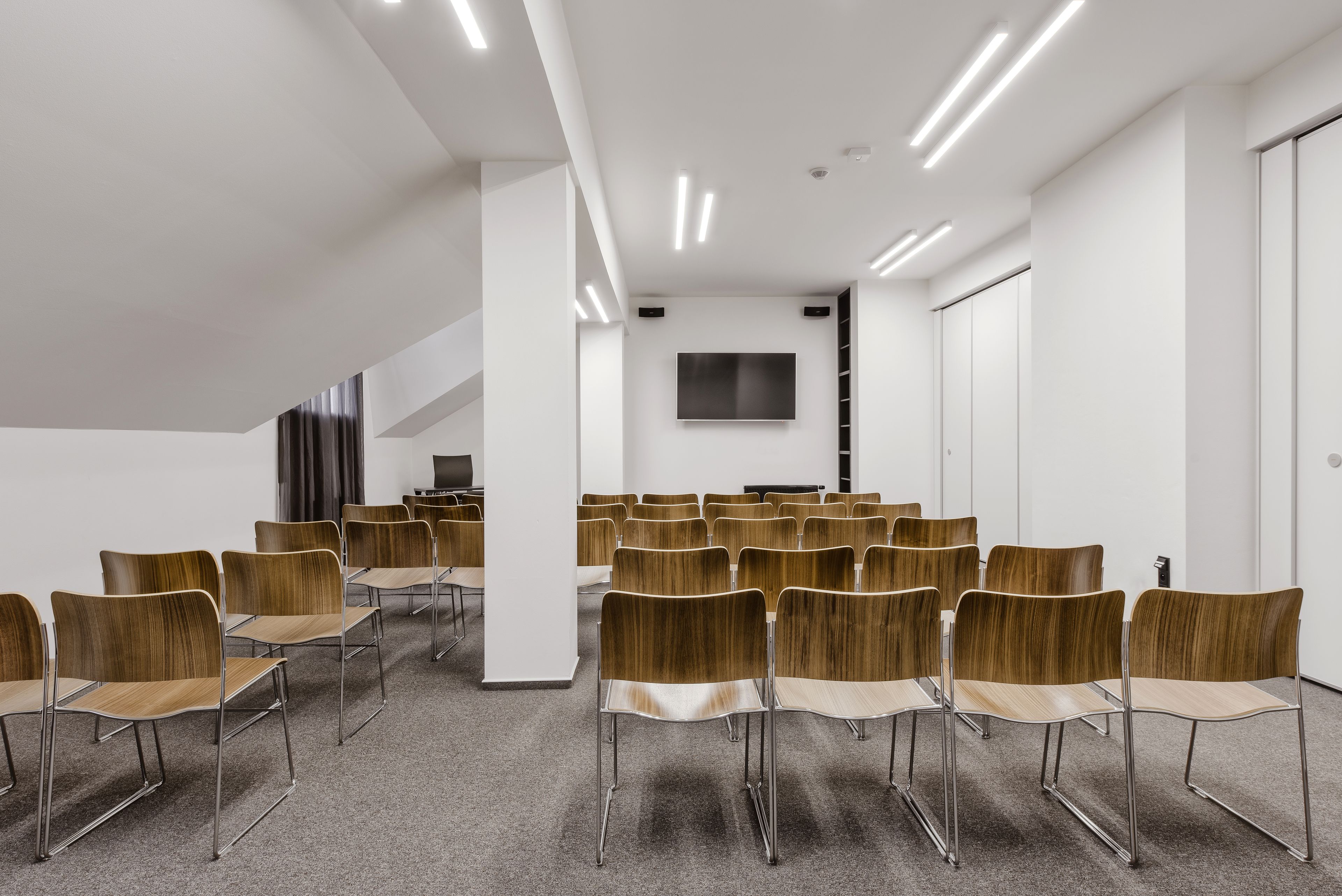 Uma sala de conferências com fileiras de cadeiras, uma TV de tela plana fixada na parede e uma escada que leva a outro andar.