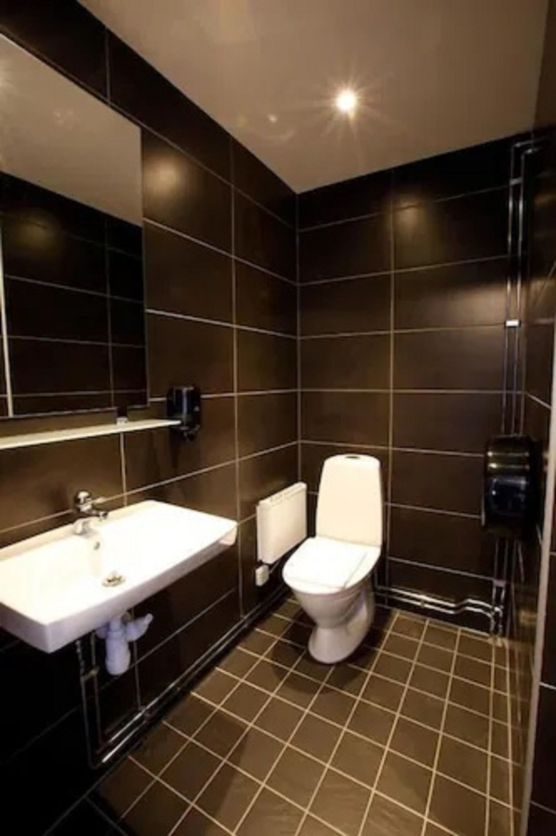 Um banheiro moderno com azulejos escuros, pia branca e vaso sanitário.
