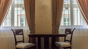 Um quarto com uma cama, duas cadeiras de madeira, uma mesa e uma janela com cortinas.