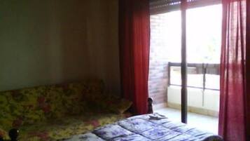 Quarto com cama, sofá e janela com cortinas vermelhas.