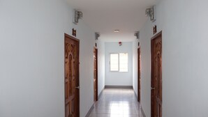 Um corredor com portas de madeira, soalho em azulejos e uma janela ao fundo.