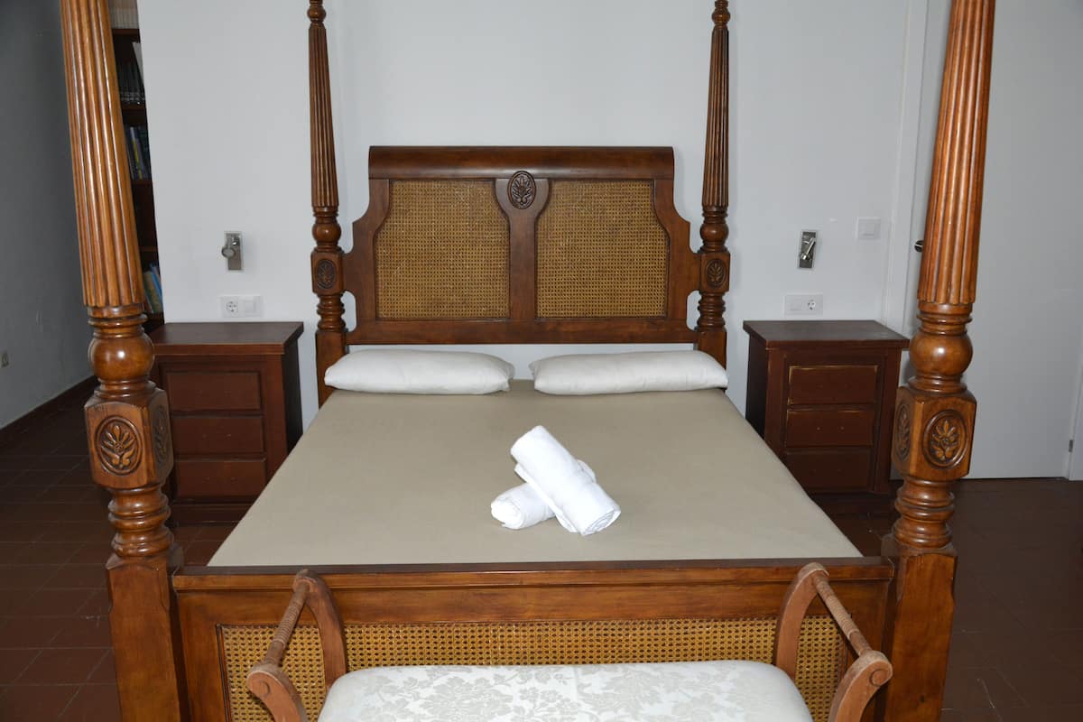 Uma cama de dossel com estrutura de madeira e cabeceira trançada.