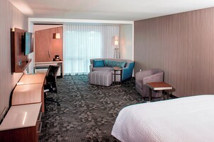 Quarto de hotel com cama, escrivaninha, cadeira, sofá e televisão.