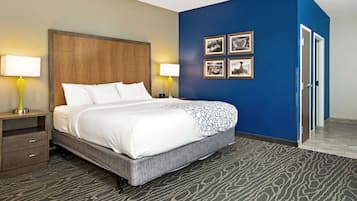 Quarto de hotel com cama, duas mesas de cabeceira com abajures, cabeceira de madeira, parede azul com quadros e carpete estampado.