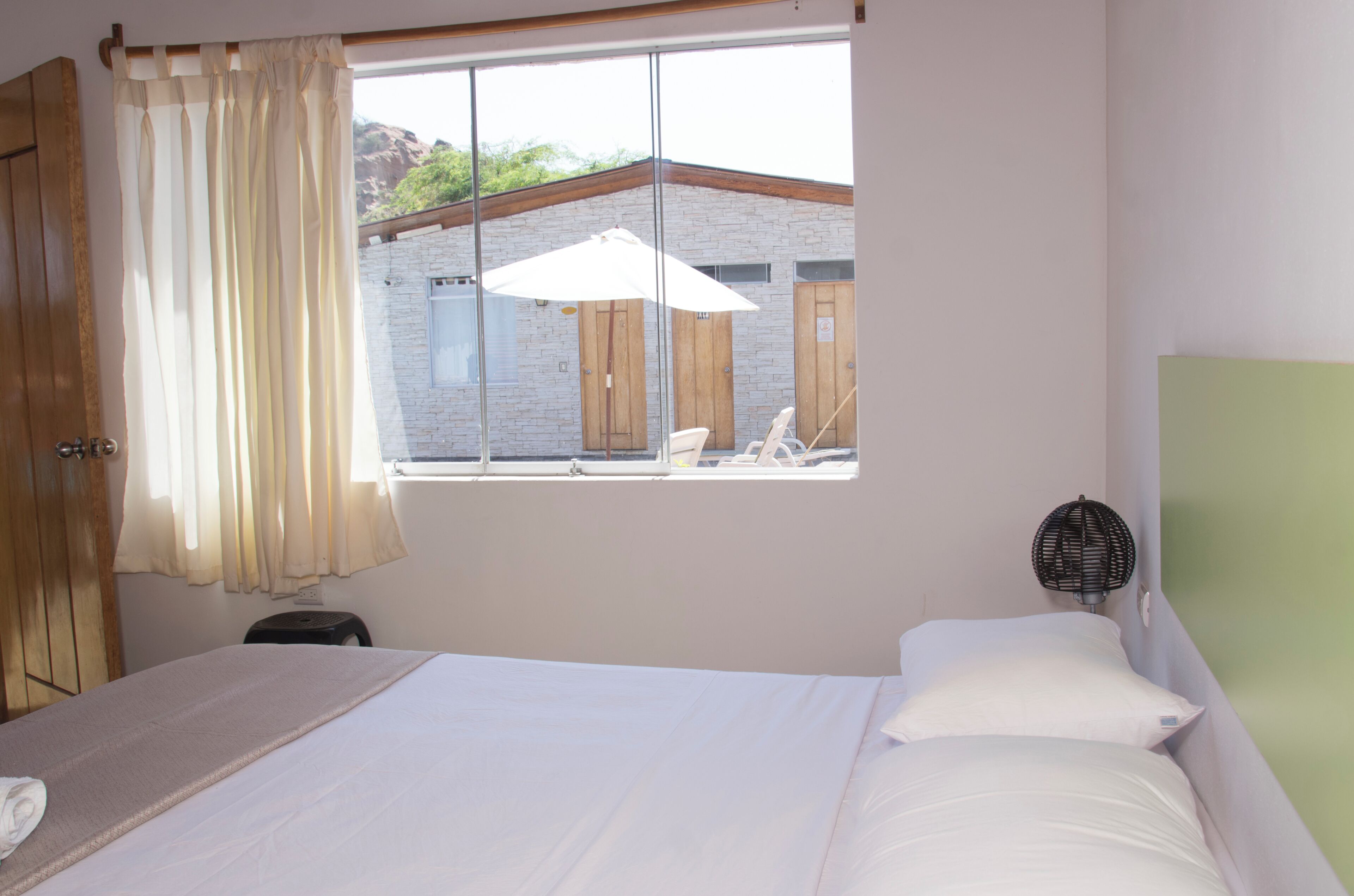 Quarto com cama, janela com cortinas, vista de um edifício e um ventilador na parede.