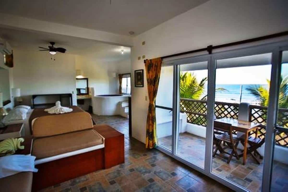 Quarto de hotel com varanda, cama, escrivaninha e vista para o oceano.