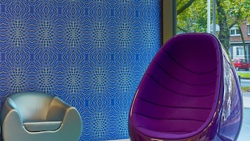 Um interior moderno com parede estampada em azul, uma cadeira roxa, uma tigela branca e um objeto vermelho no chão.