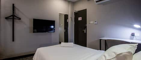 Quarto de hotel com uma cama, televisão de tela plana na parede, ar condicionado, um cabideiro e uma mesa com cadeira.