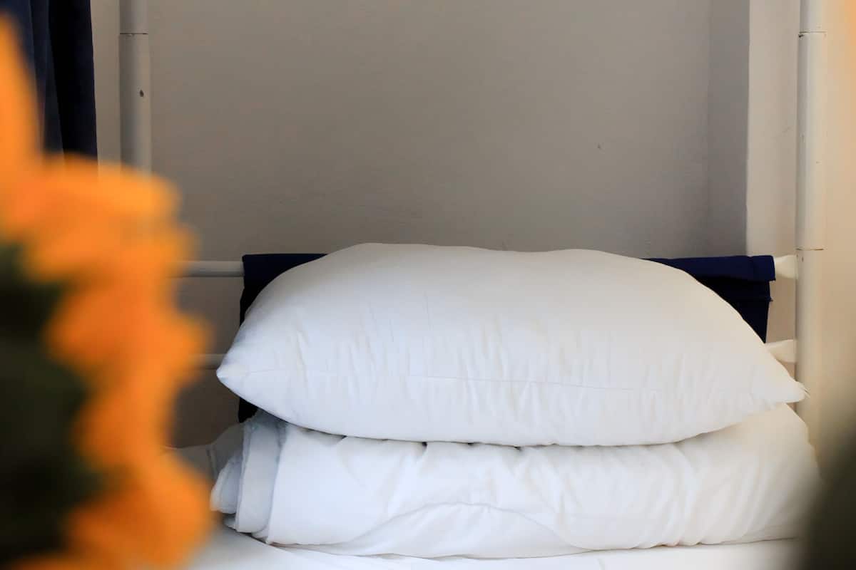 Cama com roupa de cama branca e cabeceira escura em quarto com paredes brancas.