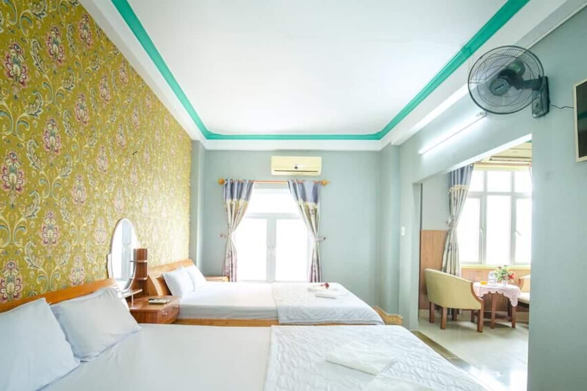 Quarto de hotel com duas camas, uma escrivaninha, uma cadeira e uma mesa.