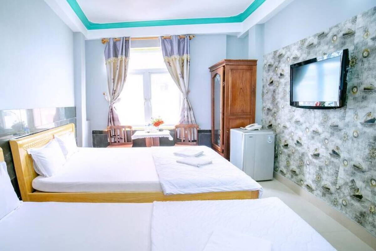 Quarto de hotel com uma cama grande, uma mesa com cadeira, uma televisão na parede e um armário.