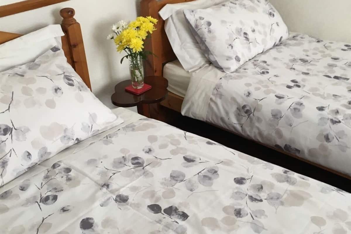 Duas camas com roupa de cama florida, um cabeceira de madeira e uma pequena mesa com um vaso de flores.