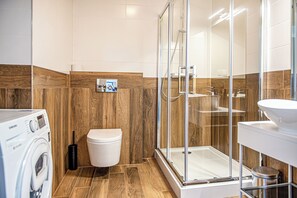 Casa de banho moderna com chuveiro em vidro, sanita branca e máquina de lavar roupa.