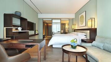 Quarto de hotel moderno com cama, sofá, escrivaninha e uma pequena mesa com um vaso de flores.