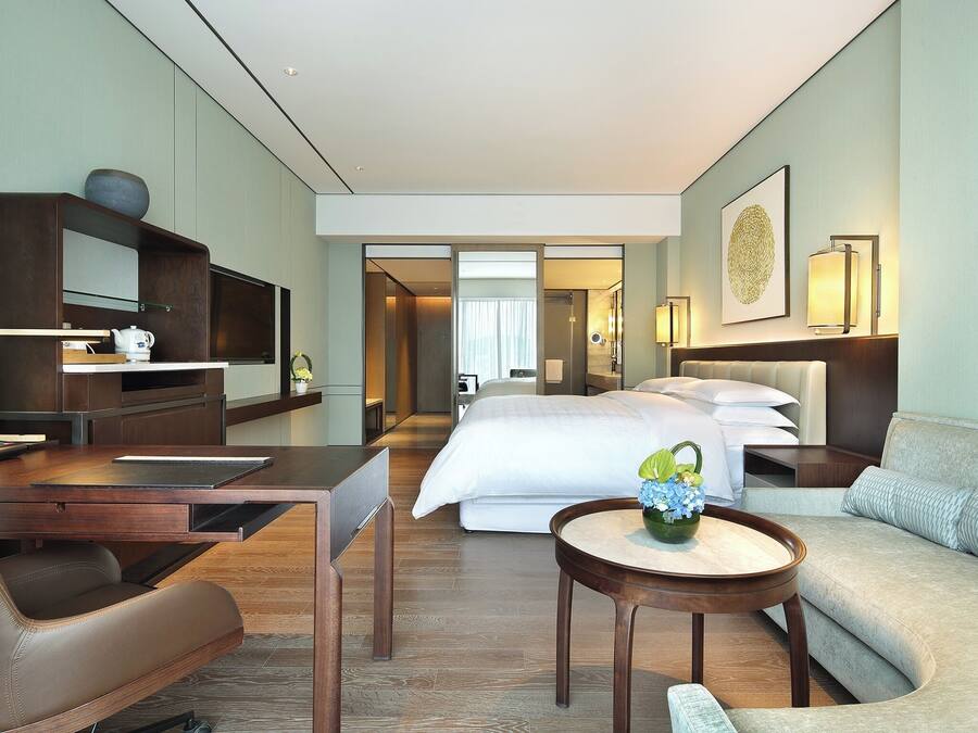 Quarto de hotel moderno com cama, sofá, escrivaninha e uma pequena mesa com um vaso de flores.
