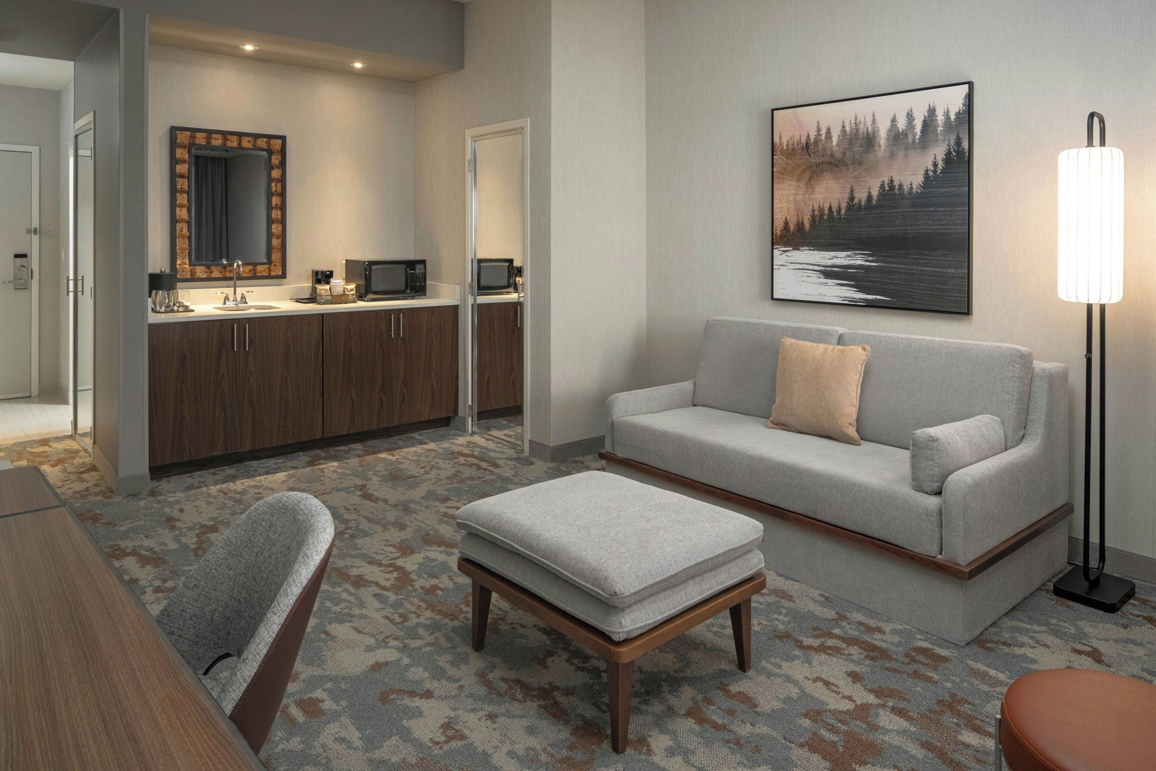 Quarto de hotel moderno com sofá, banqueta e mesa de jantar.