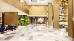 Um hall amplo com teto alto, balcão de recepção, área de estar e parede decorativa com vegetação.