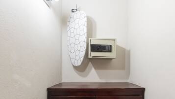 Canto de um quarto com uma cômoda de madeira, um espelho iluminado e um termostato na parede.