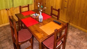 Um quarto com painéis de madeira, uma mesa de jantar, cadeiras e uma televisão na parede.