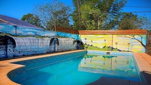 Piscina com um mural nas paredes, rodeada por um deck de madeira.