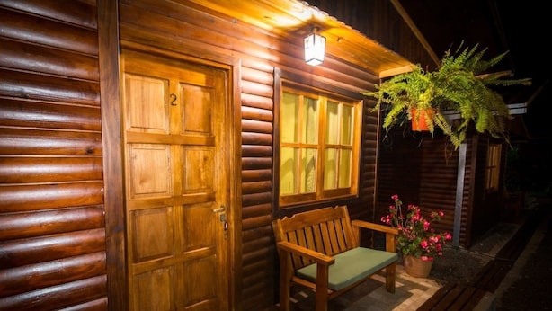 Uma cabana de madeira com o número '2' na porta, um banco na frente e vasos com plantas.
