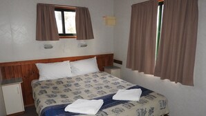 Uma cama de solteiro com colcha estampada, duas almofadas e duas mesinhas de cabeceira.